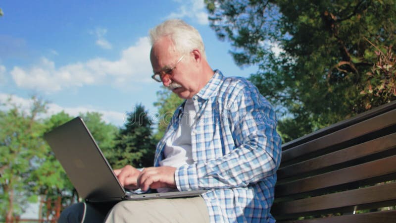 Old Man in Typing Message on Computer while Sitting on Bench in the ...