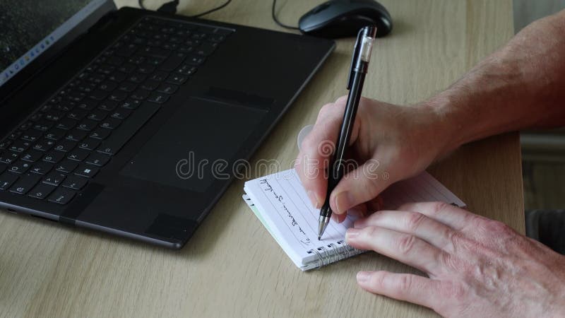 Old Man Writing Notes on Notepad Next To Computer, Close Up of Hands ...