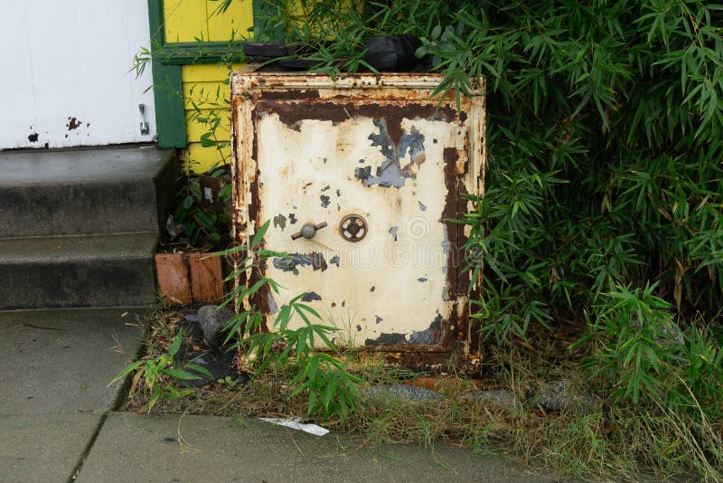 A Rusty Old Safe Sits on the Side of Building Over Grown by Plants ...