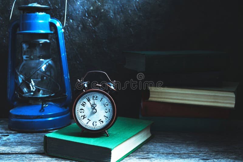 An Old Vintage Alarm Clock on a Table among Books and a Kerosene Lamp ...