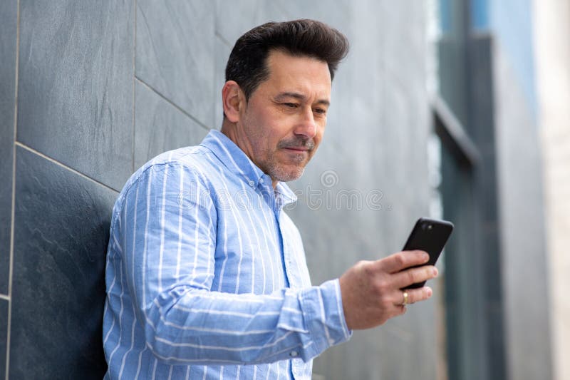 Older Man Leaning Against Wall Looking at Mobile Phone Stock Photo ...