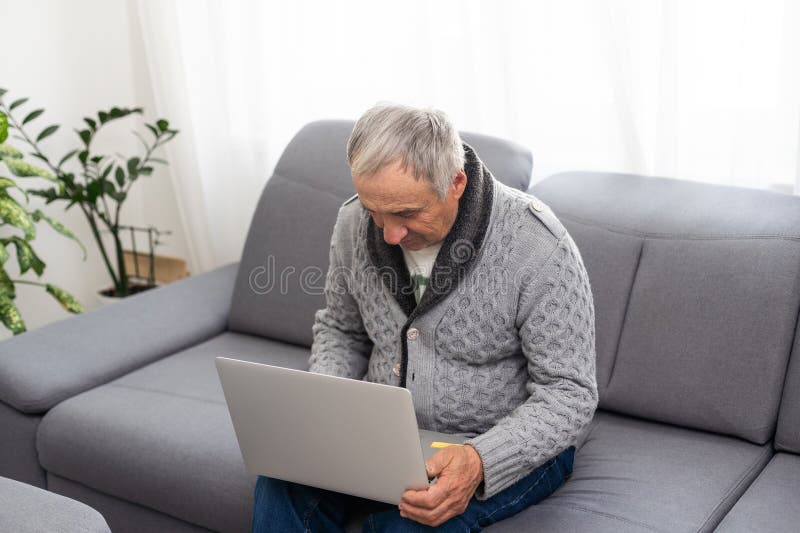 Older Man Sitting on Sofa, Smiling at Computer Screen at Home Stock ...