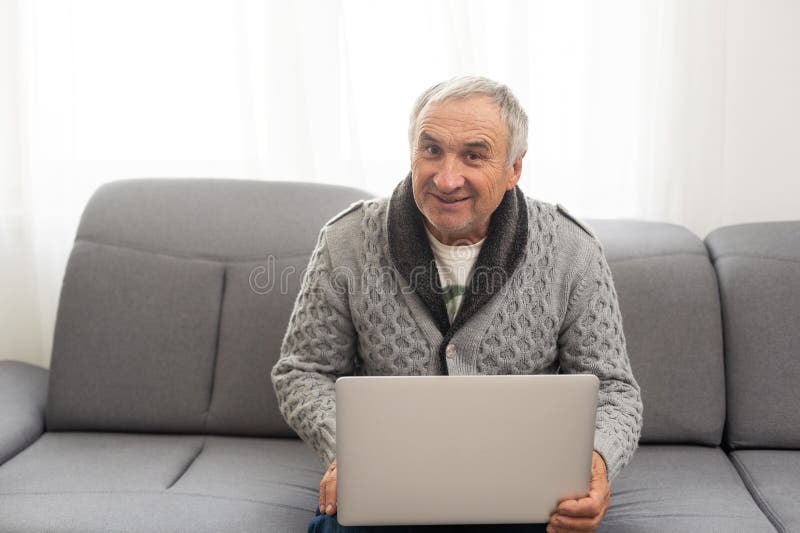 Older Man Sitting on Sofa, Smiling at Computer Screen at Home Stock ...