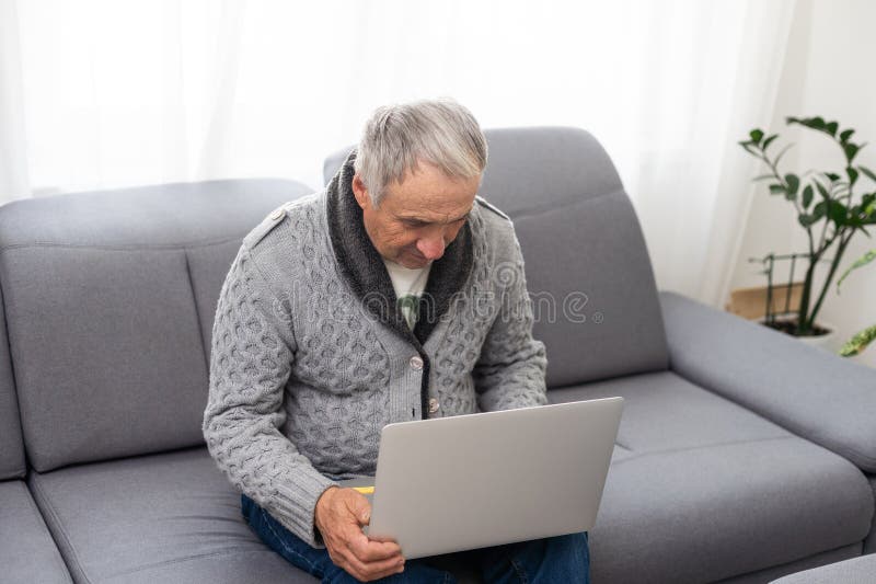 Older Man Sitting on Sofa, Smiling at Computer Screen at Home Stock ...