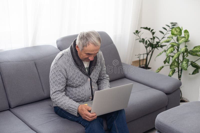Older Man Sitting on Sofa, Smiling at Computer Screen at Home Stock ...