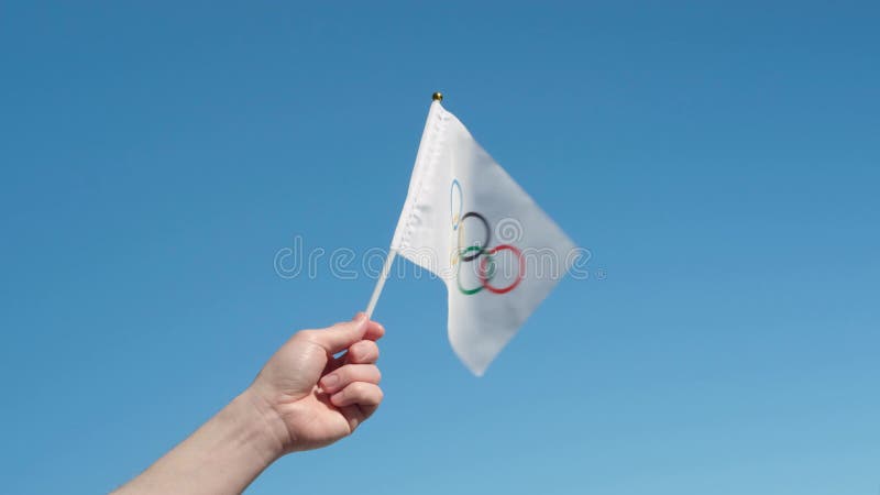 The Olympic Flag, Small in Hand, Flutters Against the Backdrop of a ...