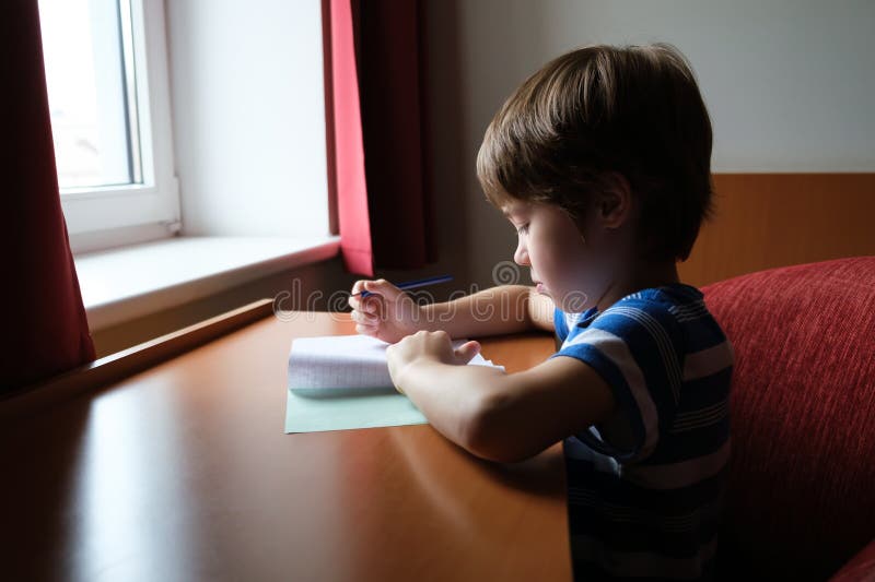 One Cute Kid is Sitting at the Table and Doing Homework. the Child ...