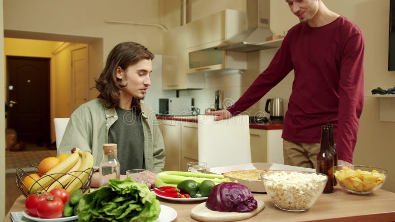 One of Friends is Sitting Down at the Table while His Pal is Entering ...