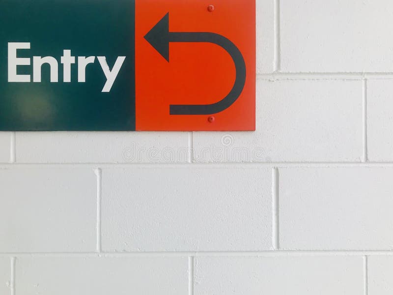 A Green Entry Sign with a Red Arrow Indicates on White Brick Wall ...