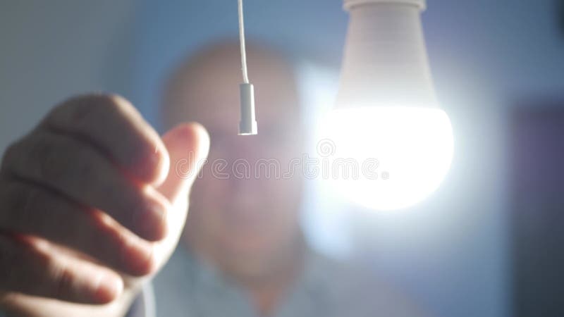 One Person Pull the Switch Cord and Turns on the Light Bulb in a Dark ...