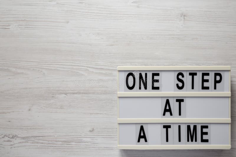 `One Step at a Time` on a Lightbox on a White Wooden Background, Top ...