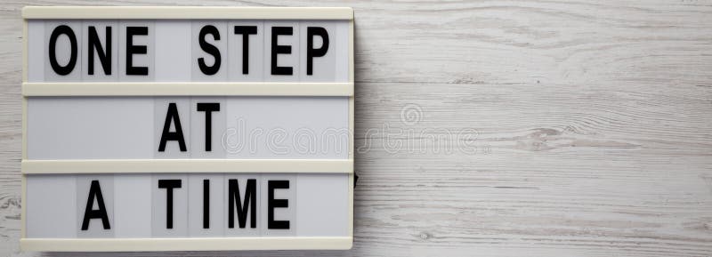 `One Step at a Time` on a Lightbox on a White Wooden Surface, Overhead ...