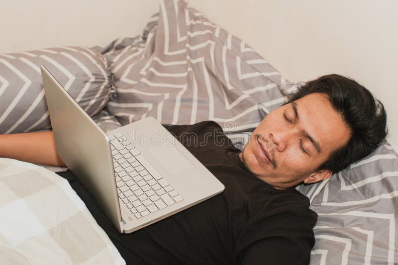 Always Online. a Southeast Asian Man Sleeping on Bed while Working on ...