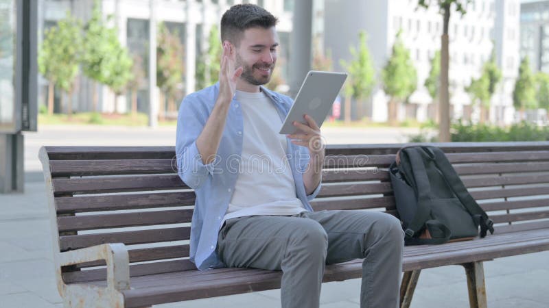 Online Video Chat on Tablet by Young Man Sitting on Bench Stock Image ...