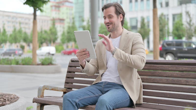 Online Video Chat on Tablet by Young Man Sitting on Bench Stock Photo ...