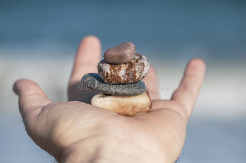Open Hand with a Stack of Four Pebbles of Different Colors on a Beach ...