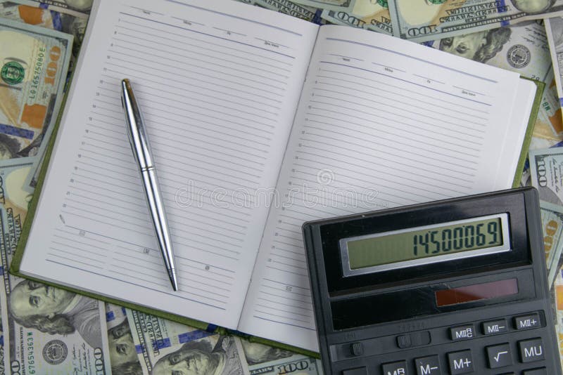 An Open Notebook with a Pen and Calculator Stand on a Pile of Dolar ... An Open Notebook with a Pen and Calculator Stand on a Pile of Dolar ...