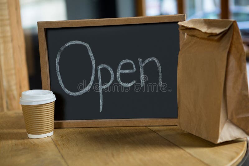 Open Signboard with Disposable Coffee Cup and Paper Bag on Table Stock ...