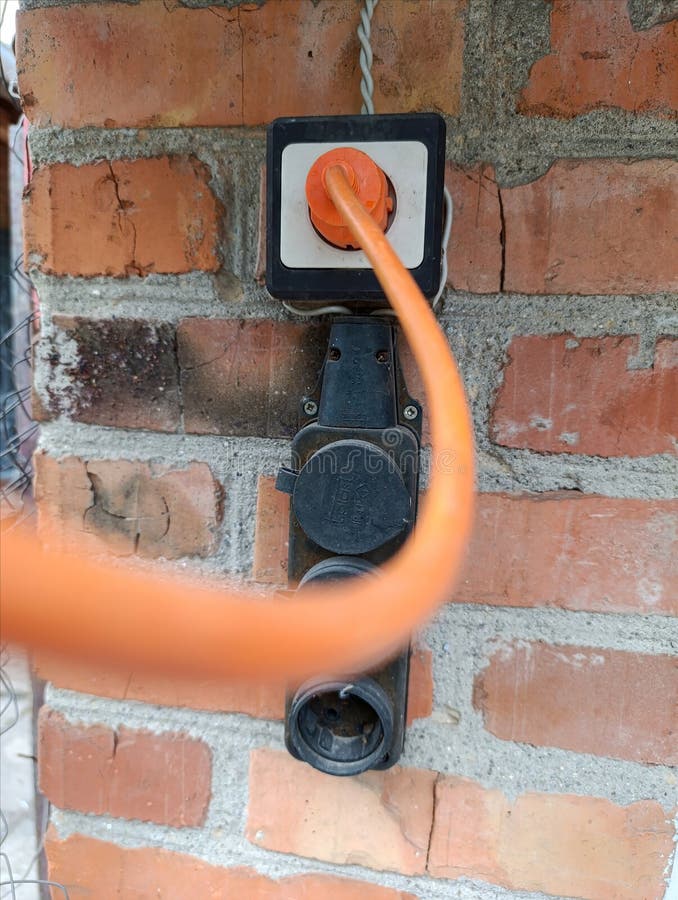 An Orange Cable Connected To an Electrical Outlet on a Brick Wall Stock ...