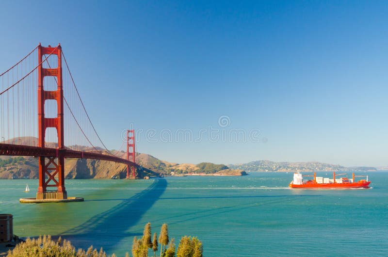 An Orange Container Ship with Cranes Passing Under the Golden Ga Stock ...
