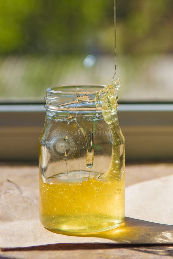 Organic Pure Honey in Jar on Window Sill. Stream of Honey Stock Photo ...
