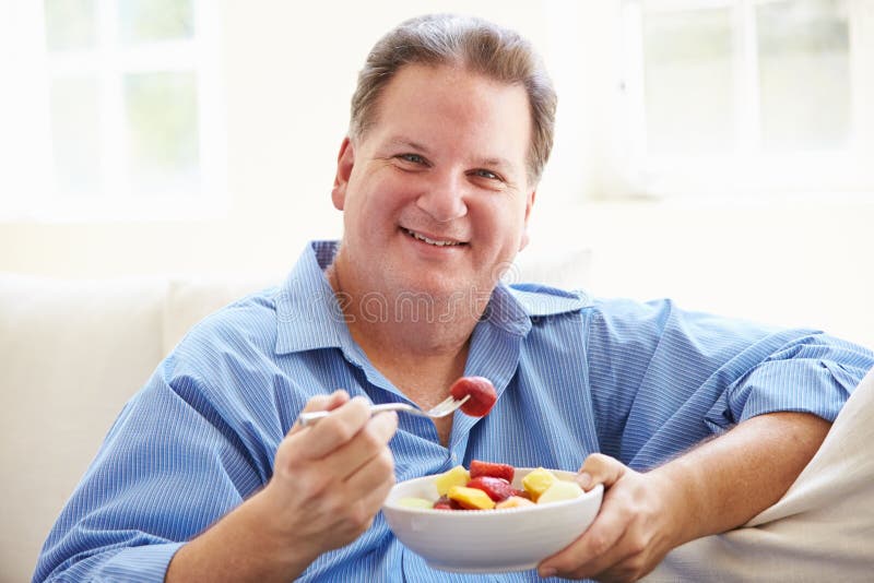Overweight Man Sitting on Sofa Eating Bowl of Fresh Fruit Stock Photo ...