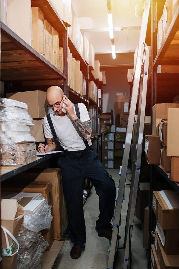 Overworked Male Warehouse Worker Talking on the Phone, Writing on a ...