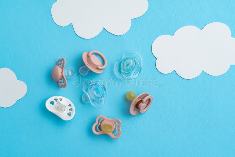 Pacifiers on Blue Background with White Paper Cut Out Clouds and Copy ...