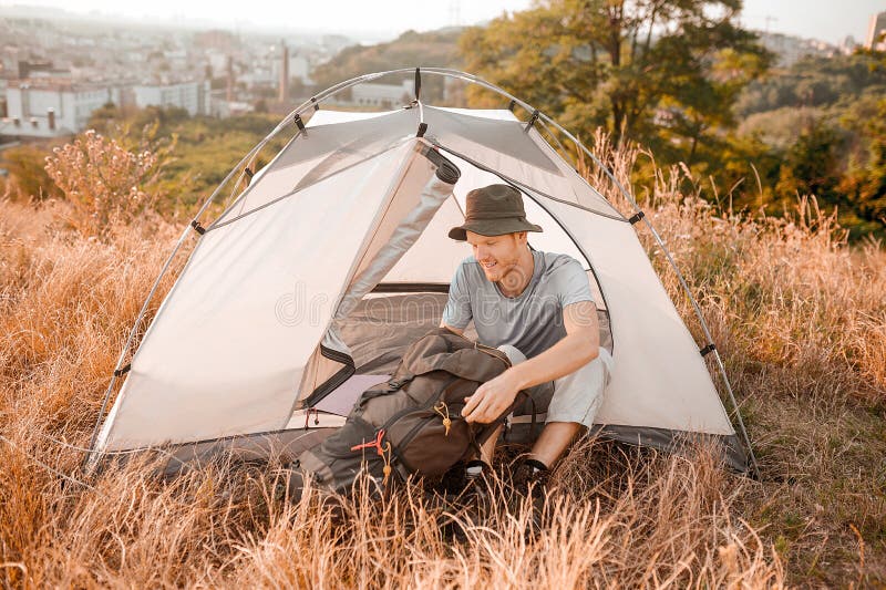 A Man in a Hat Packing His Backpack while Sitting Near the Tent Stock ...