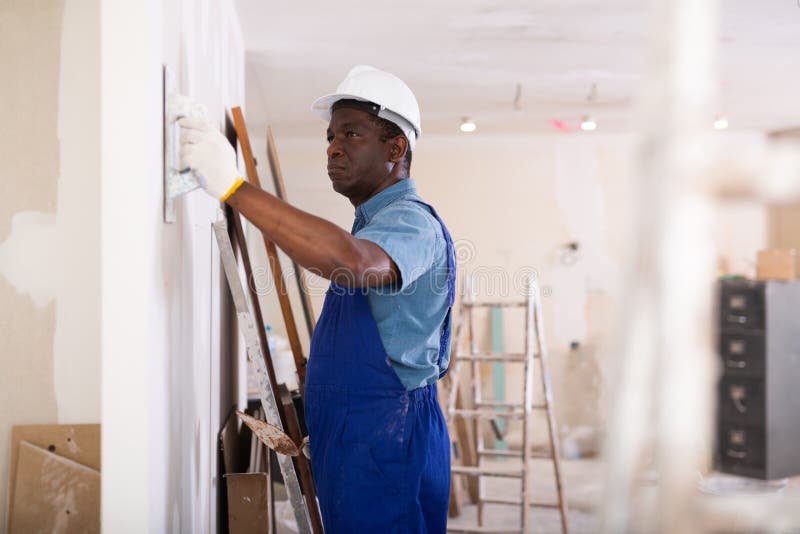 Painter in Blue Overalls Leveling Plaster on the Wall with Spatula ...