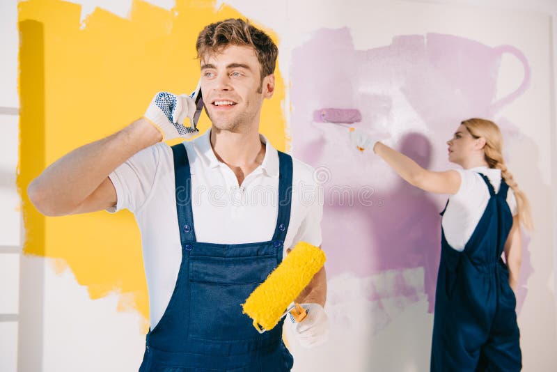 Painter Talking on Smartphone while Attractive Colleague Painting Wall ...