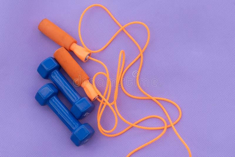 A Pair of Blue Dumbbells and an Orange Jump Rope are Placed on a Purple ...