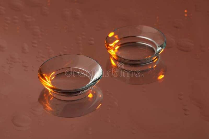Pair of Contact Lenses on Wet Brown Reflective Surface Stock Photo ...