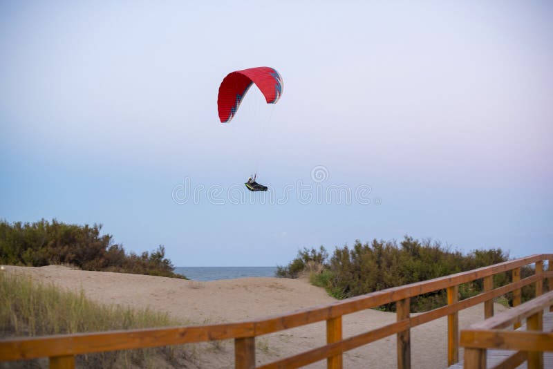 Paraglider with a Vibrant Red Canopy Approaching the Beach at Dusk ...