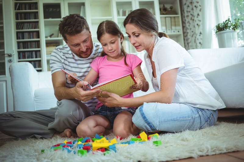 Parents and Daughter Reading a Book while Playing with Building Blocks ...