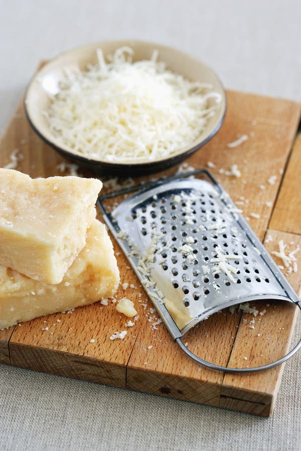 Parmesan Cheese and Grater on Cutting Board at Table Stock Photo ...