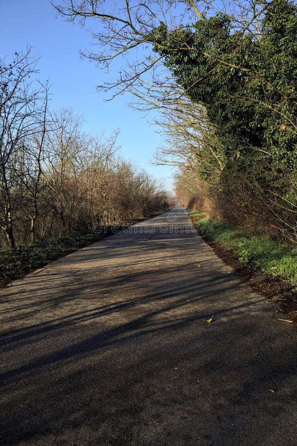 Paved Path Bordered by a Field and a Stream of Water with a Pylon Afar ...