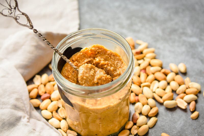 Peanut Paste in an Open Jar and and Spoon, Peanuts on the Gray Table ...