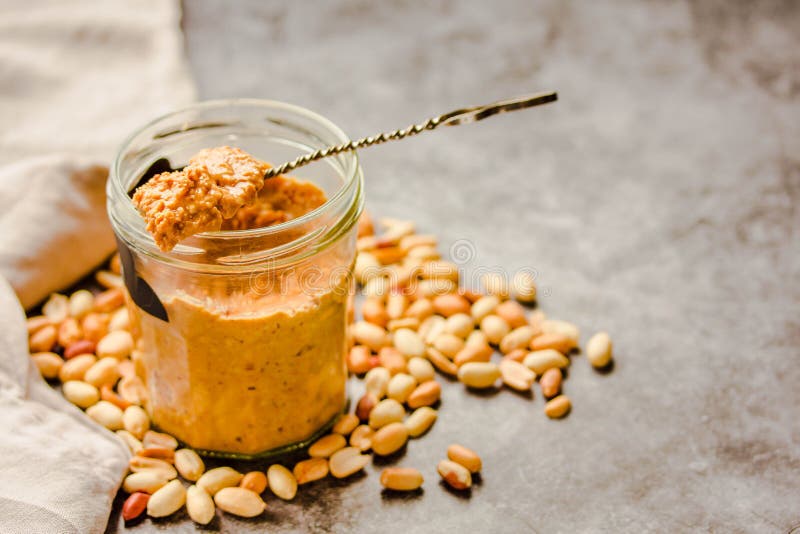 Peanut Paste in an Open Jar and and Spoon, Peanuts on the Gray Table ...
