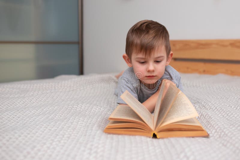 Pensive Little Boy Lying on the Bed Reading a Book at Home. Vacation ... Pensive Little Boy Lying on the Bed Reading a Book at Home. Vacation ...
