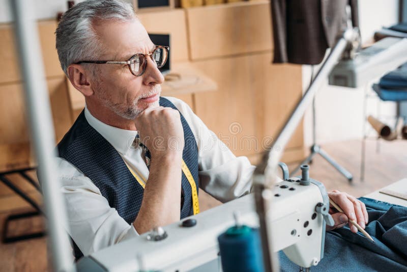 Pensive Tailor Sitting at a Table with Hand on Chin in a Sewing ...
