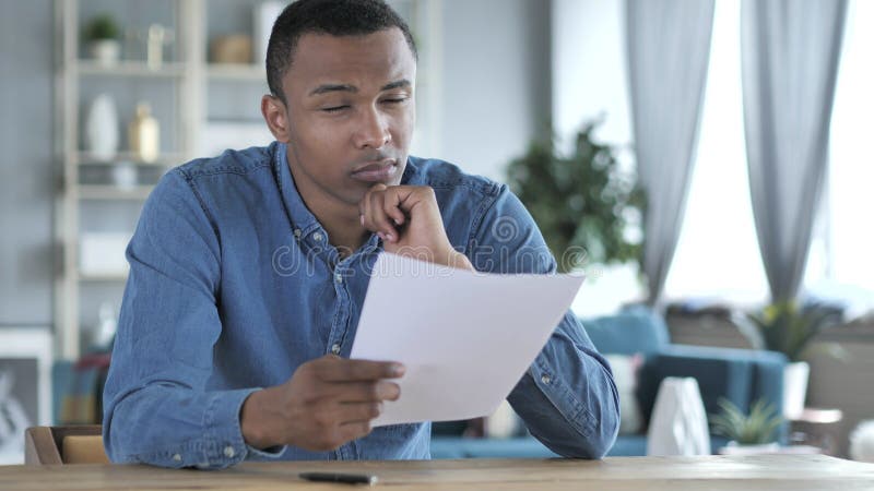 Pensive Young African Man Reading and Writing on Documents, Paperwork ...