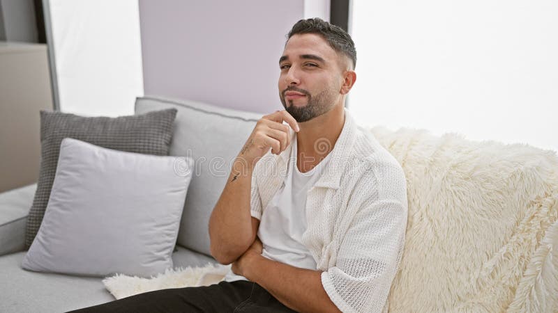 Pensive Young Arabian Man Doubtfully Thinking on Sofa at Home, Hand on ...
