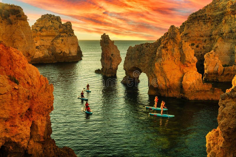 People on Paddleboards Out at Sunset in Front of Rock Formations Stock ...
