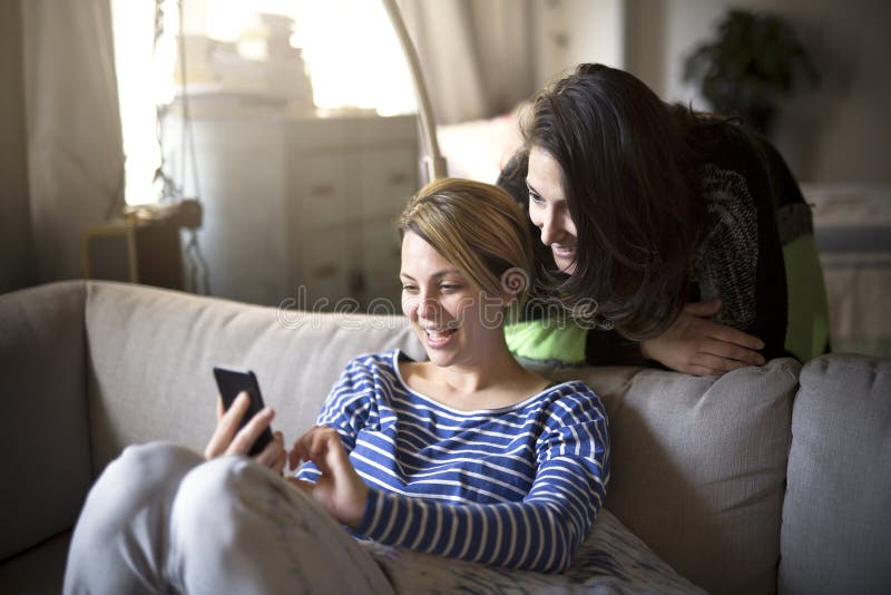 People Relations. Two Girls are Speaking and Using Cellphone on Sofa ...