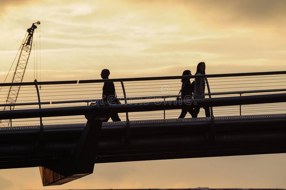 People Walking on Bridge at Sunset with Crane in Background Stock Image ...