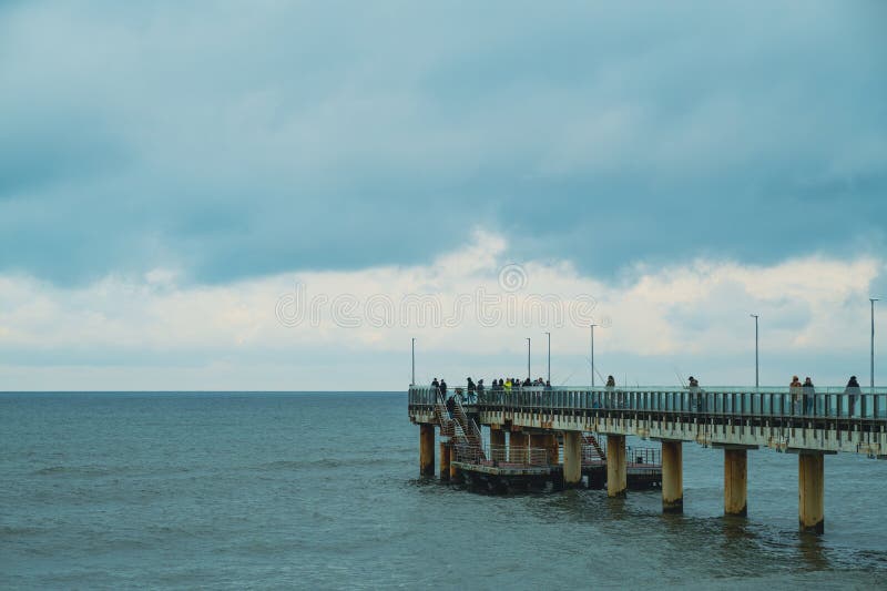 People Walking on a Pier Overlooking the Ocean at Dusk with Dramatic ...