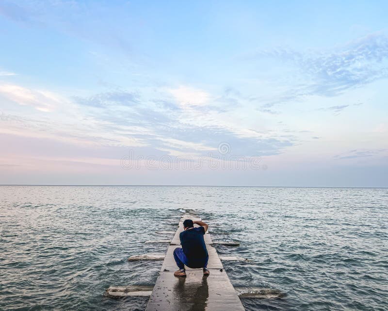 Person Crouching on a Pier Over the Ocean during Sunset with a Clear ...