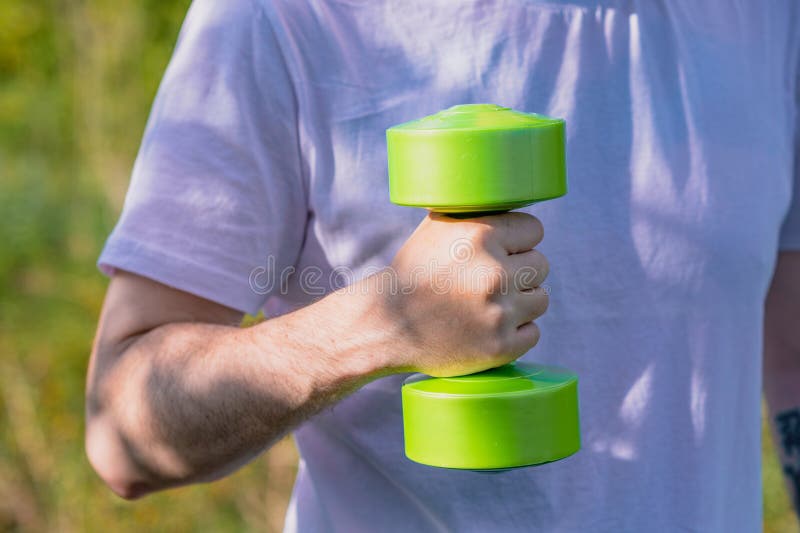 Person Exercising Outdoors with a Green Dumbbell in a Park during ...