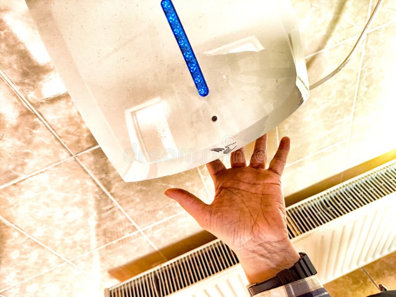 A Person Places Their Hand Under a Hand Dryer in a Restroom, Utilizing ...